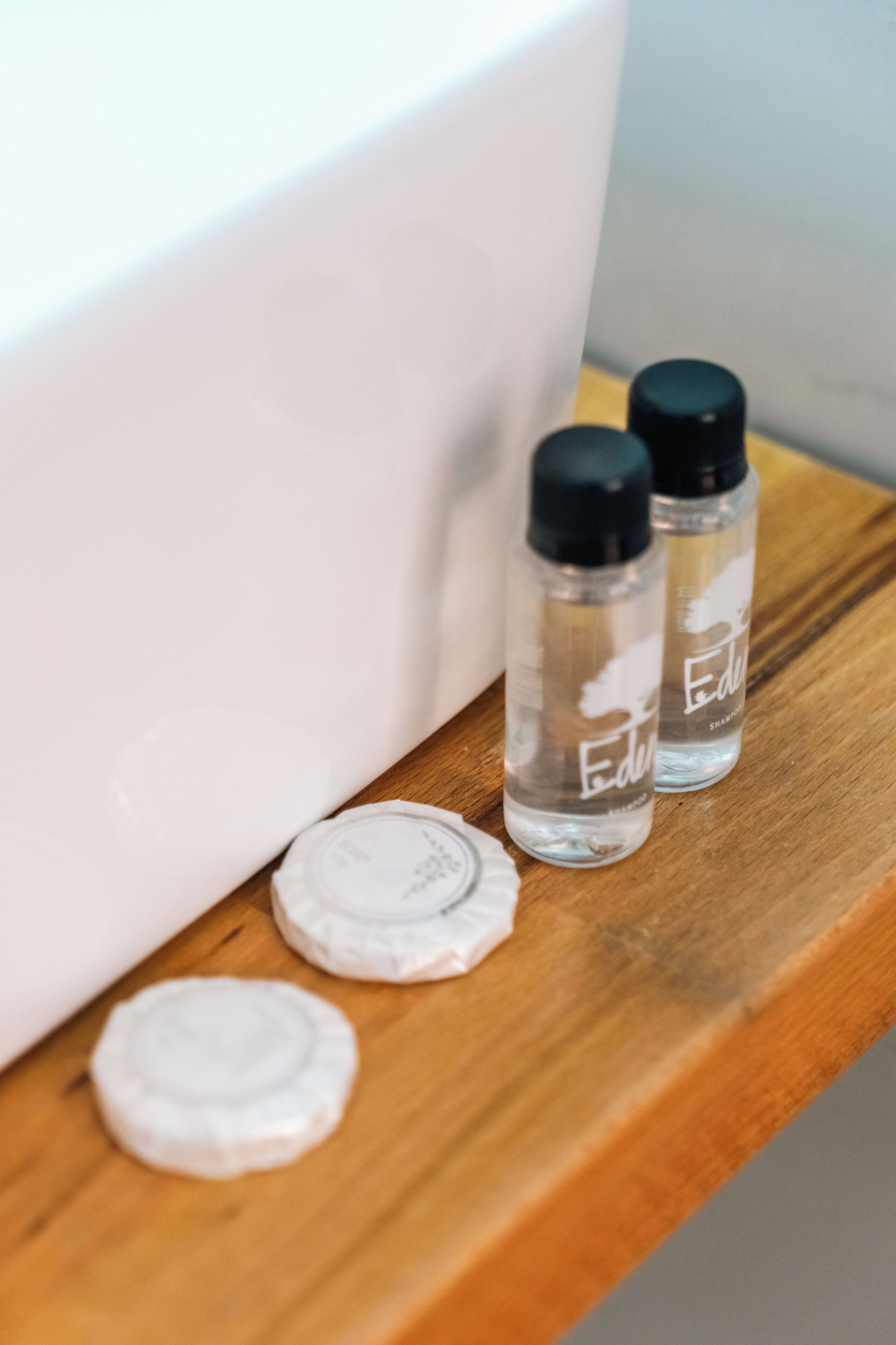 Estante de madeira com duas garrafas transparentes rotuladas 'Eden' e um objeto branco com um desenho circular.
