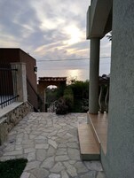 Um pátio com piso de pedra e vista para o mar, com uma pérgula e um muro de pedra.