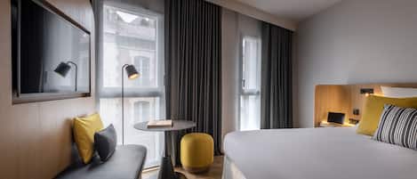 Quarto de hotel moderno com uma cama grande, uma mesa pequena, um banco e um sofá.