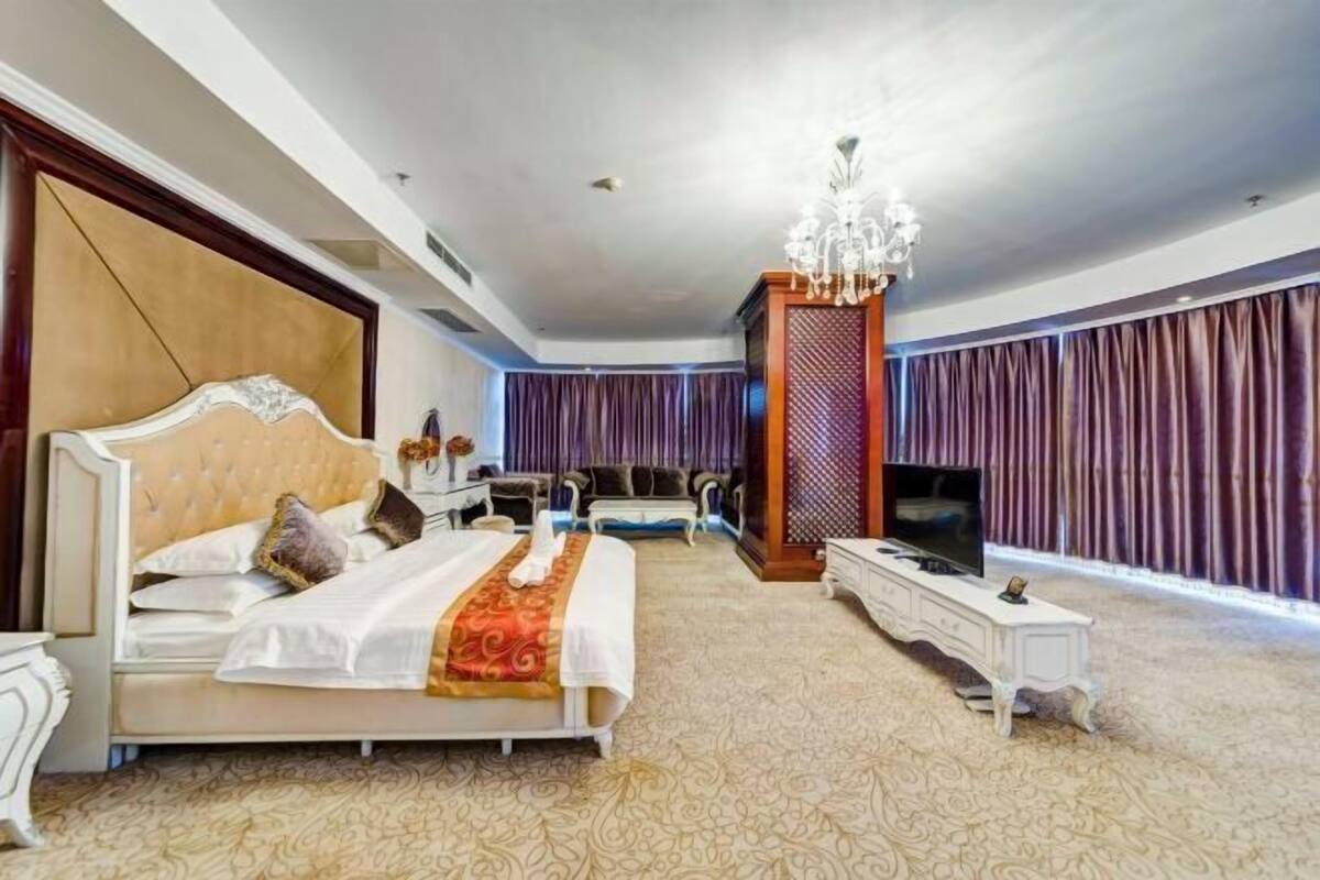 Quarto de hotel com uma cama grande, televisão, escrivaninha e um candelabro.