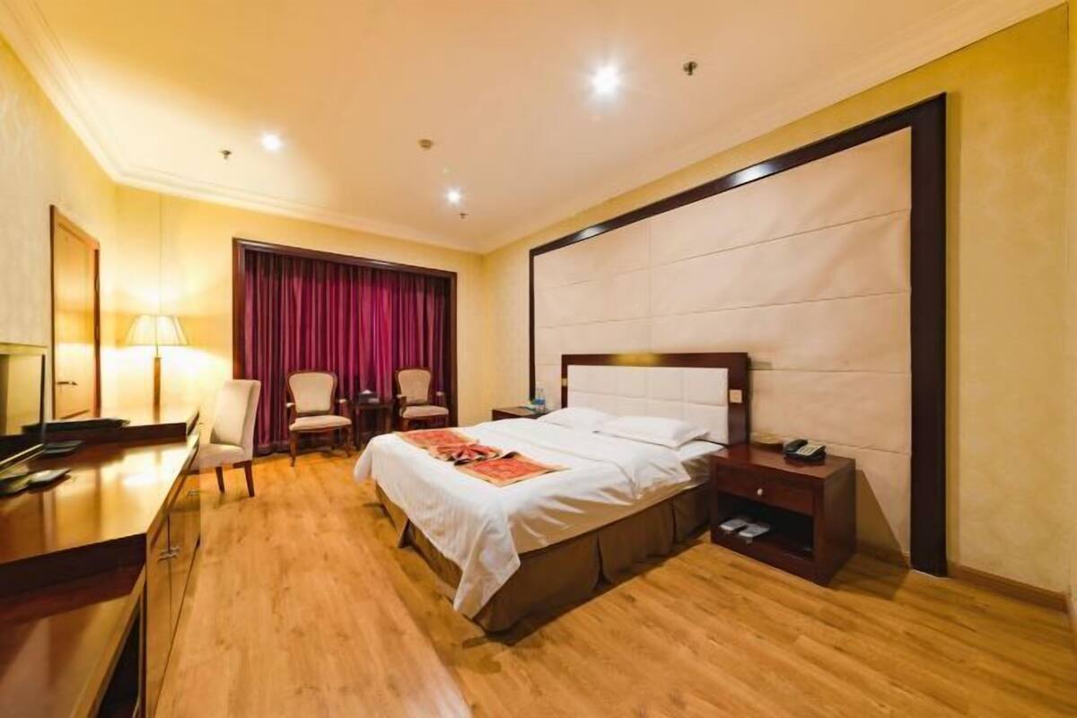 Quarto de hotel com cama, mesa de cabeceira, luminária e escrivaninha com cadeira.