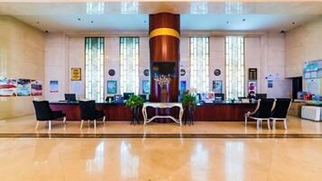 Um hall amplo com balcão de atendimento, duas cadeiras pretas, uma mesa central com plantas e um grande pilar de madeira.
