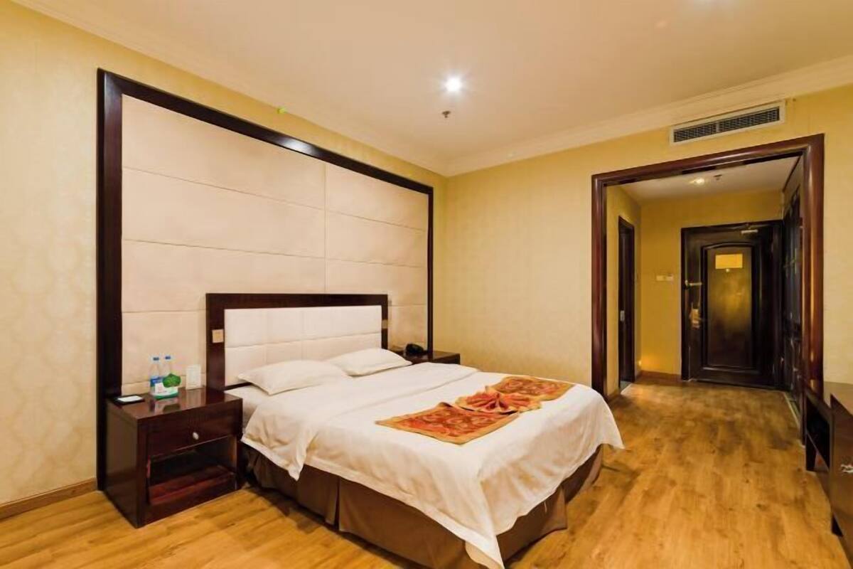 Quarto de hotel com uma cama grande, uma mesa de cabeceira, piso de madeira e uma porta que dá para outro quarto.