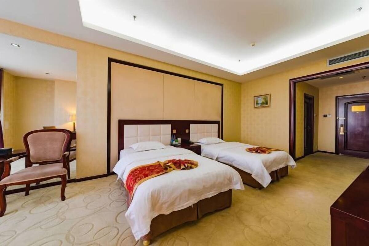 Quarto de hotel com duas camas, uma mesa, uma cadeira e uma porta.