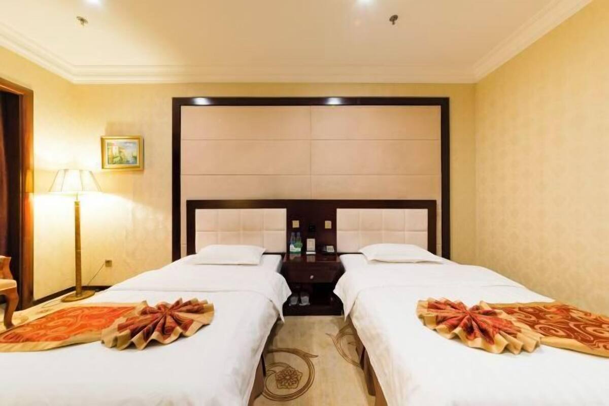 Quarto de hotel com duas camas, uma mesa de cabeceira, um abajur e um quadro na parede.