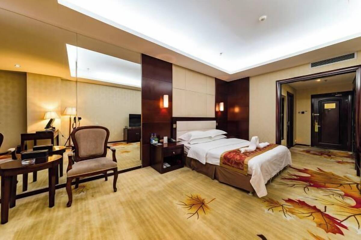 Quarto de hotel com cama, escrivaninha, cadeira, mesa de cabeceira e espelho.