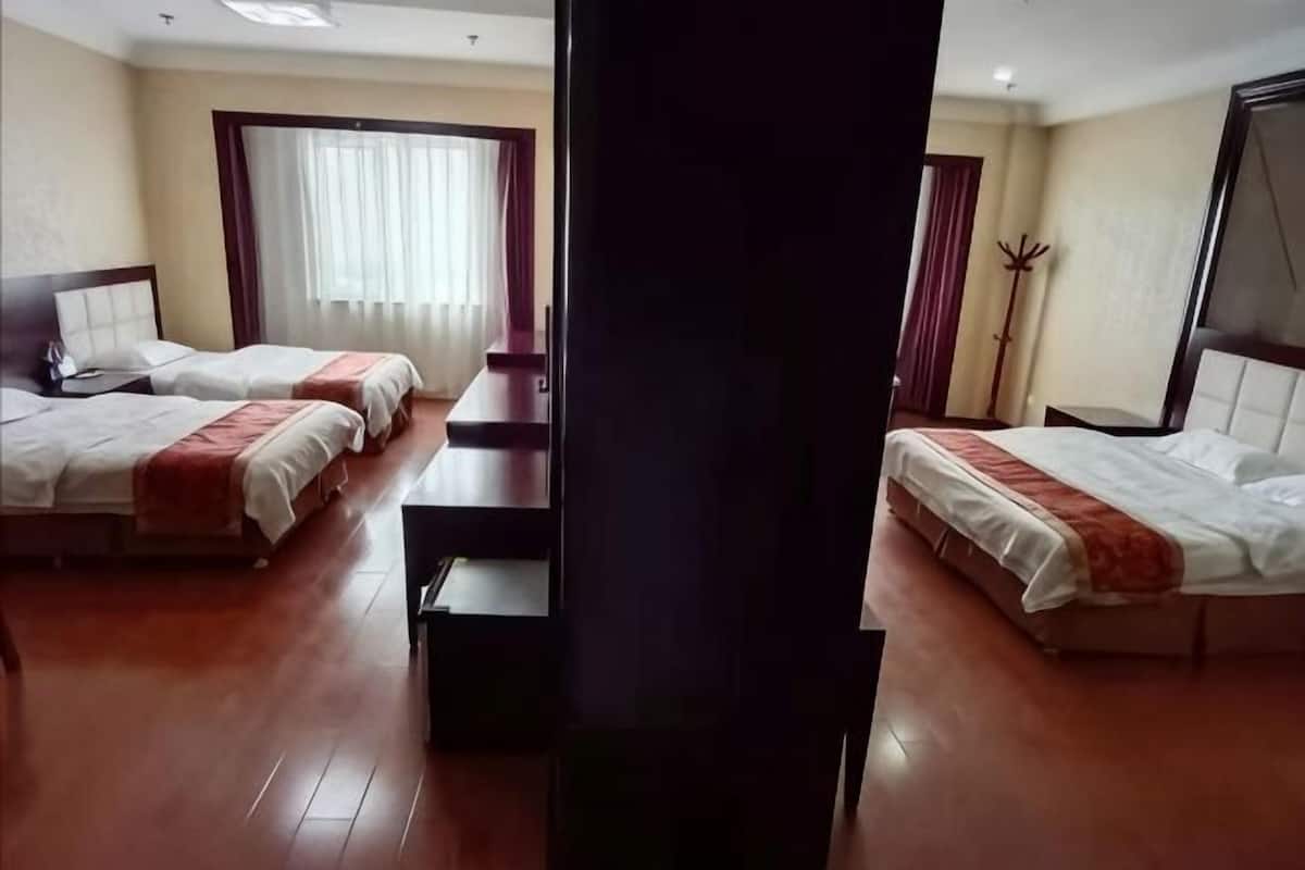 Quarto de hotel com duas camas, uma escrivaninha e uma janela grande com cortinas.