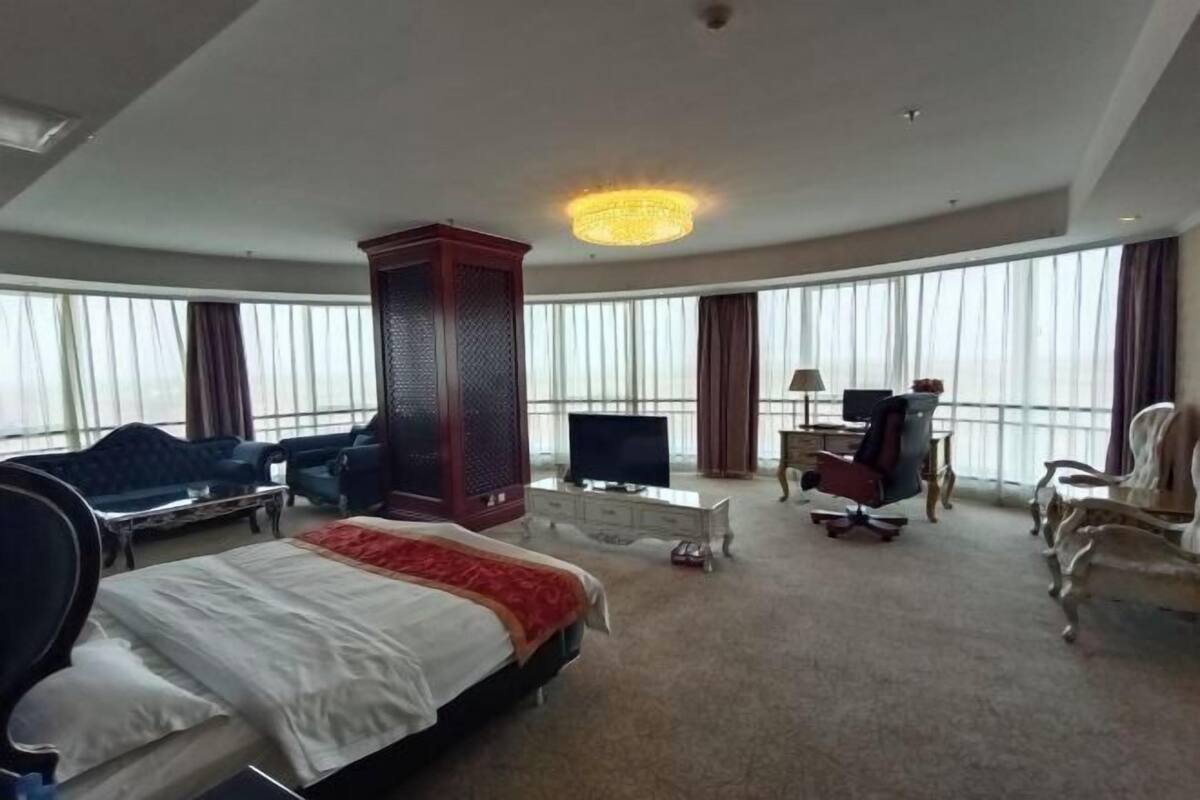 Quarto de hotel com cama, dois sofás, televisão, escrivaninha e lustre.