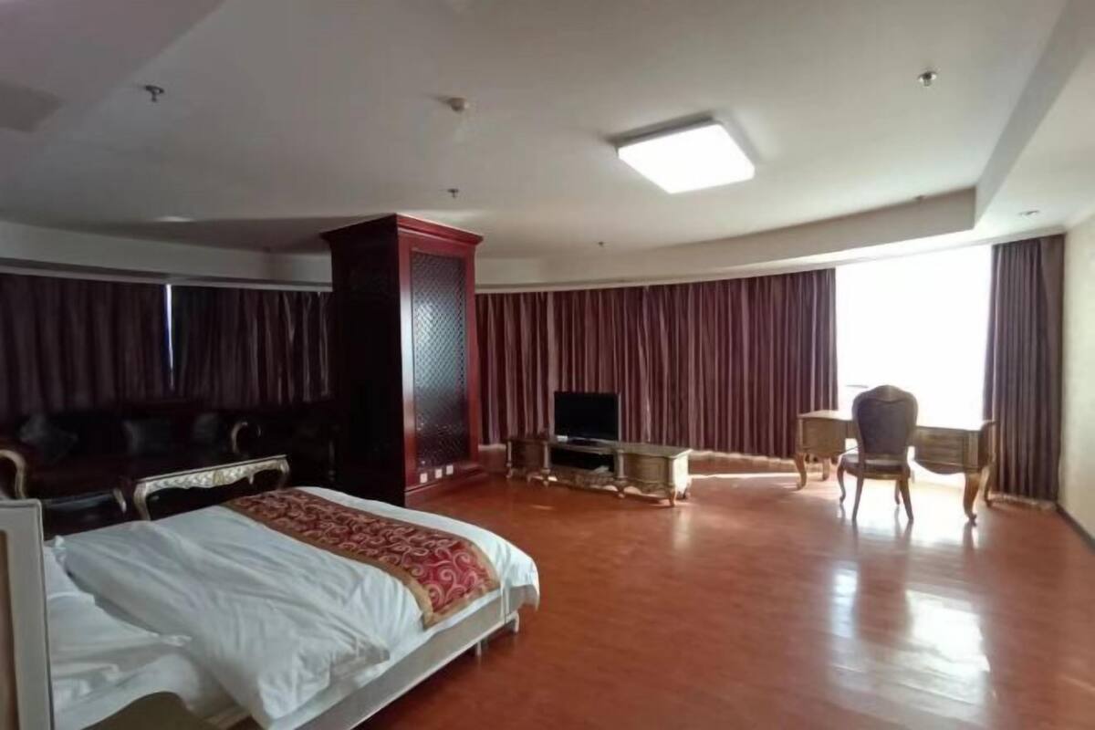 Quarto de hotel com uma cama, televisão, secretária e uma cadeira.
