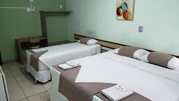 Quarto de hotel com duas camas, uma cadeira, uma mesinha e um aparelho de ar condicionado na parede.