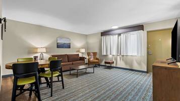 Quarto de hotel com área de estar, incluindo sofá, cadeiras, mesa de centro, televisão e janela com cortinas.