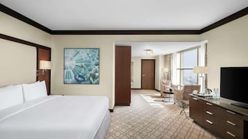 Quarto de hotel com uma cama grande, uma escrivaninha com televisão, uma cadeira e uma janela ampla.
