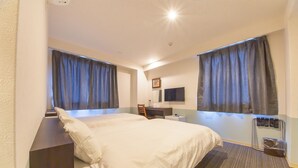 Quarto de hotel com uma cama, escrivaninha, cadeira, televisão e janela com cortinas.