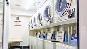 Uma lavanderia com várias máquinas de lavar e secar, uma pequena mesa e placas de instruções.