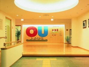 Um saguão de hotel com uma placa grande 'OU LAND', uma mesa de recepção e piso de azulejos.
