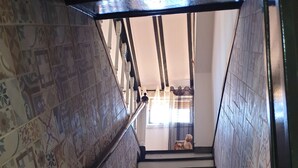 Uma escadaria com azulejos decorativos nas paredes, que leva a um quarto com janela e cortinas.