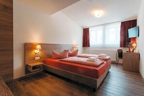 Quarto de hotel com cama, abajures, televisão e janela com cortinas.