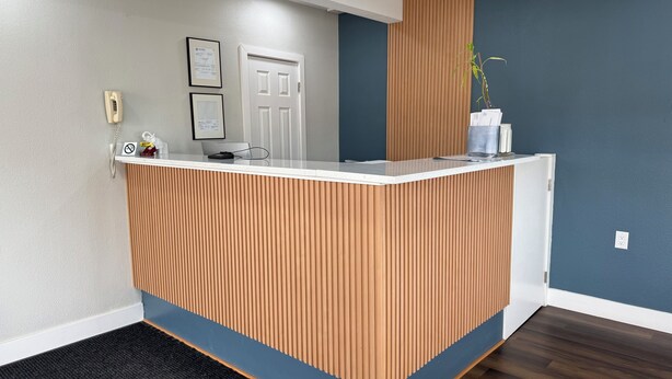 Uma receção com design em painel de madeira, um telefone, certificados emoldurados e uma porta ao fundo.