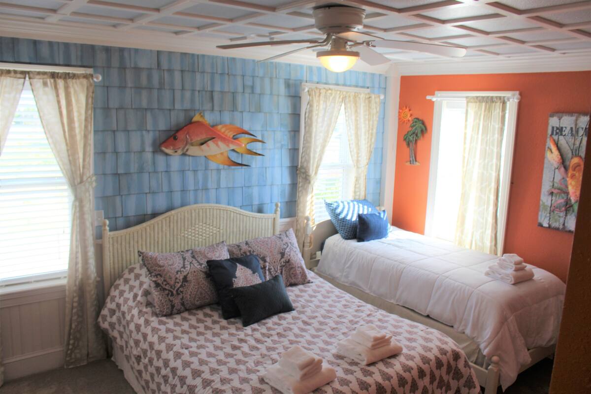 Quarto com duas camas, um ventilador de teto e uma decoração de peixe na parede.