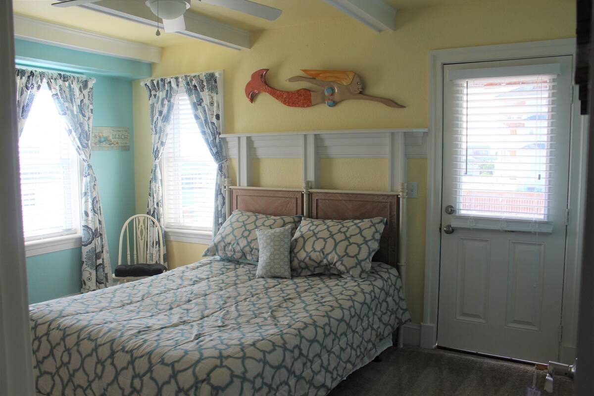 Quarto com cama, cadeira, porta e um objeto decorativo na parede.