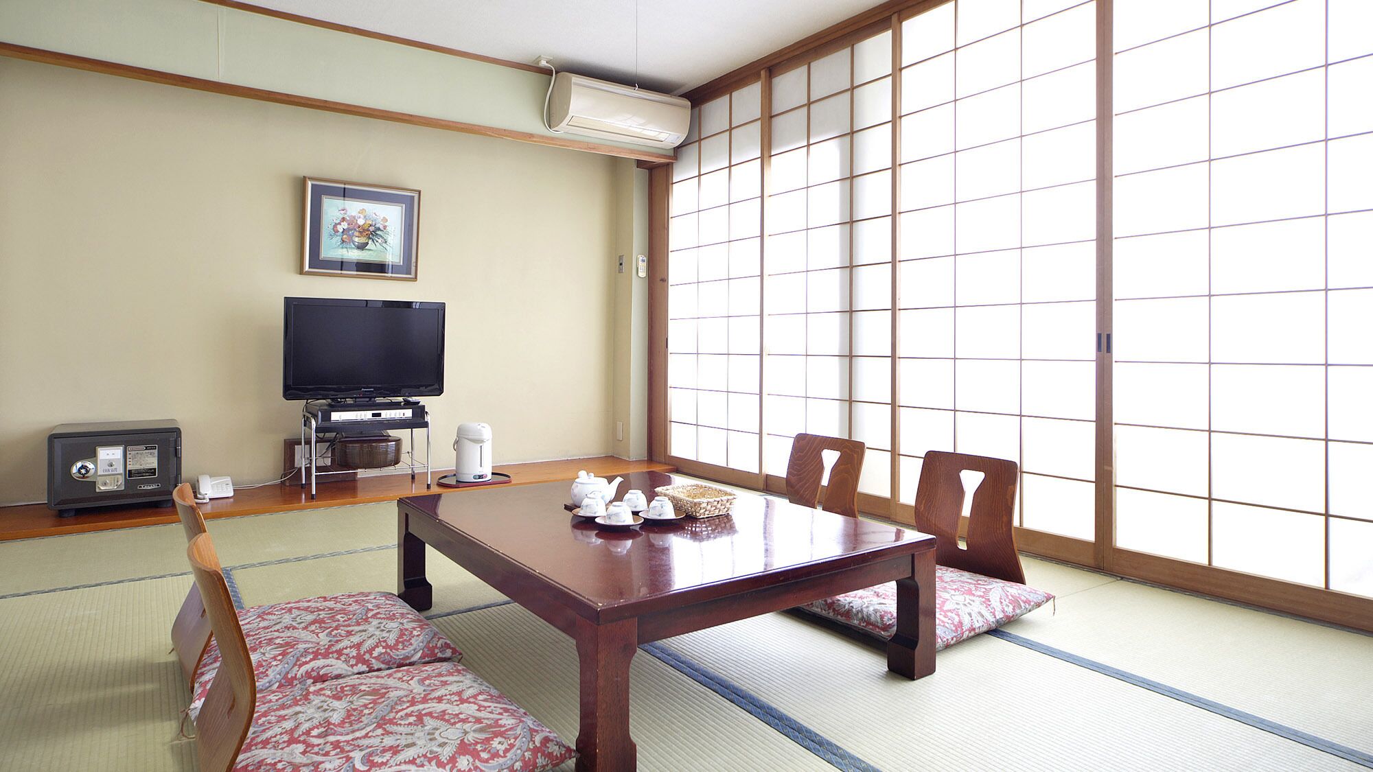 Um quarto japonês tradicional com tatames, uma mesa baixa com chá, uma televisão e uma cama futon.