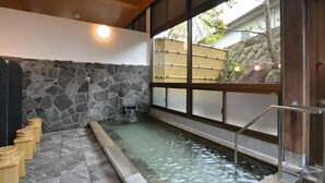 Um onsen japonês tradicional com parede de pedra, teto de madeira e vista para uma cerca de bambu.