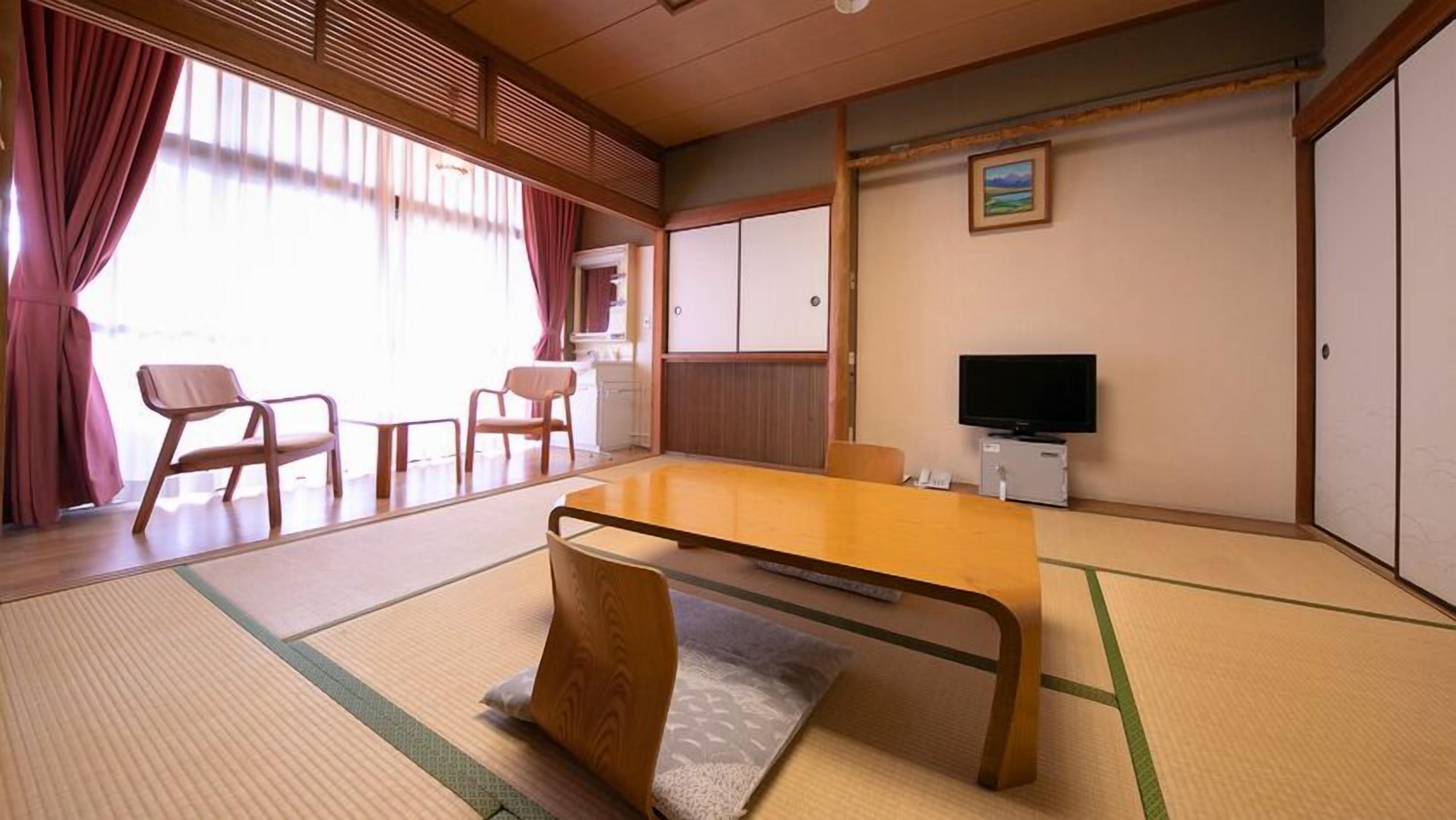 Um quarto japonês tradicional com tatames, uma mesa baixa, cadeiras, uma televisão e portas deslizantes.