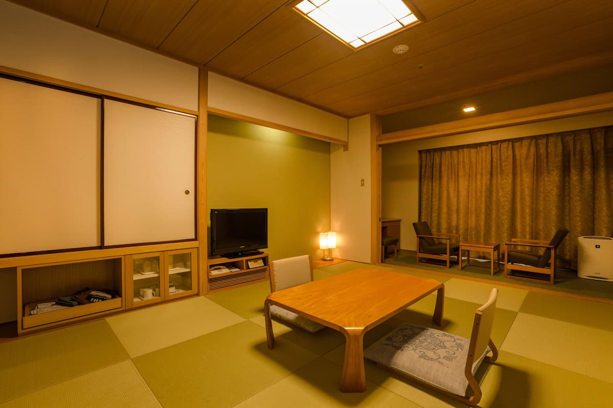 Uma sala de estar tradicional japonesa com tatames, uma mesa de madeira baixa e uma televisão.