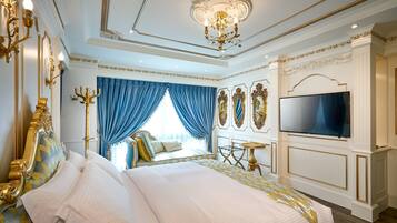 Um quarto luxuoso com uma cama grande, móveis dourados elaborados, um candelabro e uma televisão.