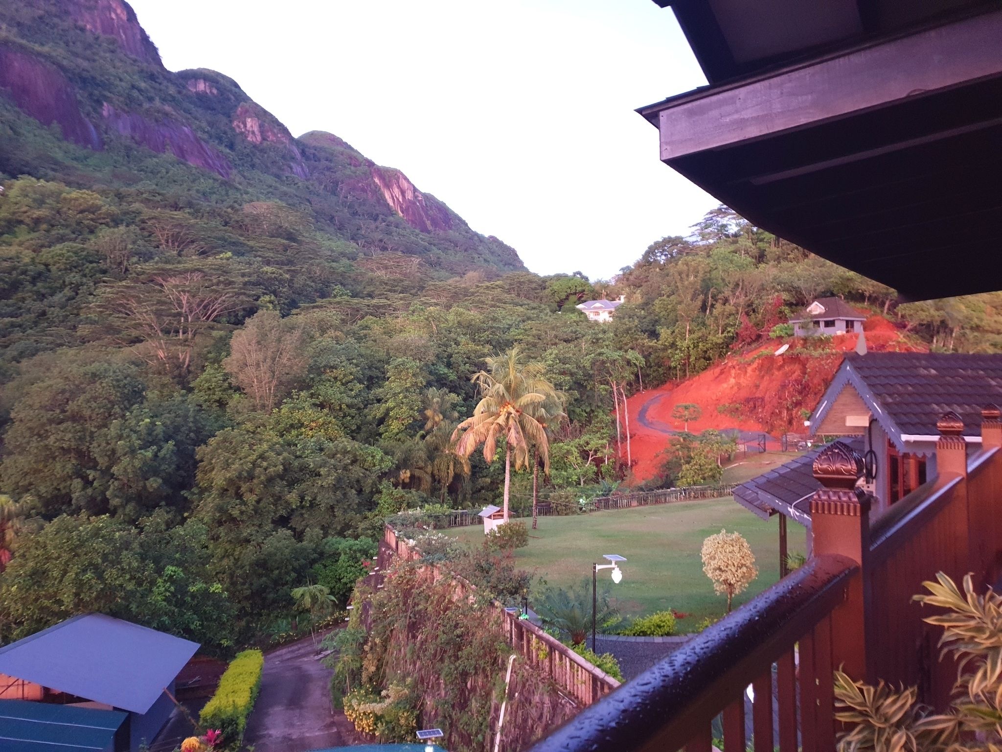 Zona residencial com uma casa rodeada por vegetação exuberante e uma montanha ao fundo.