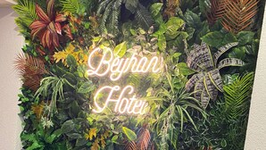 Paredes decoradas com diversas plantas verdes e um letreiro de neon que diz "Beyron Hotel".