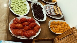 Mesa de buffet com diversos alimentos, incluindo pepinos fatiados, azeitonas pretas, tomates e queijo.