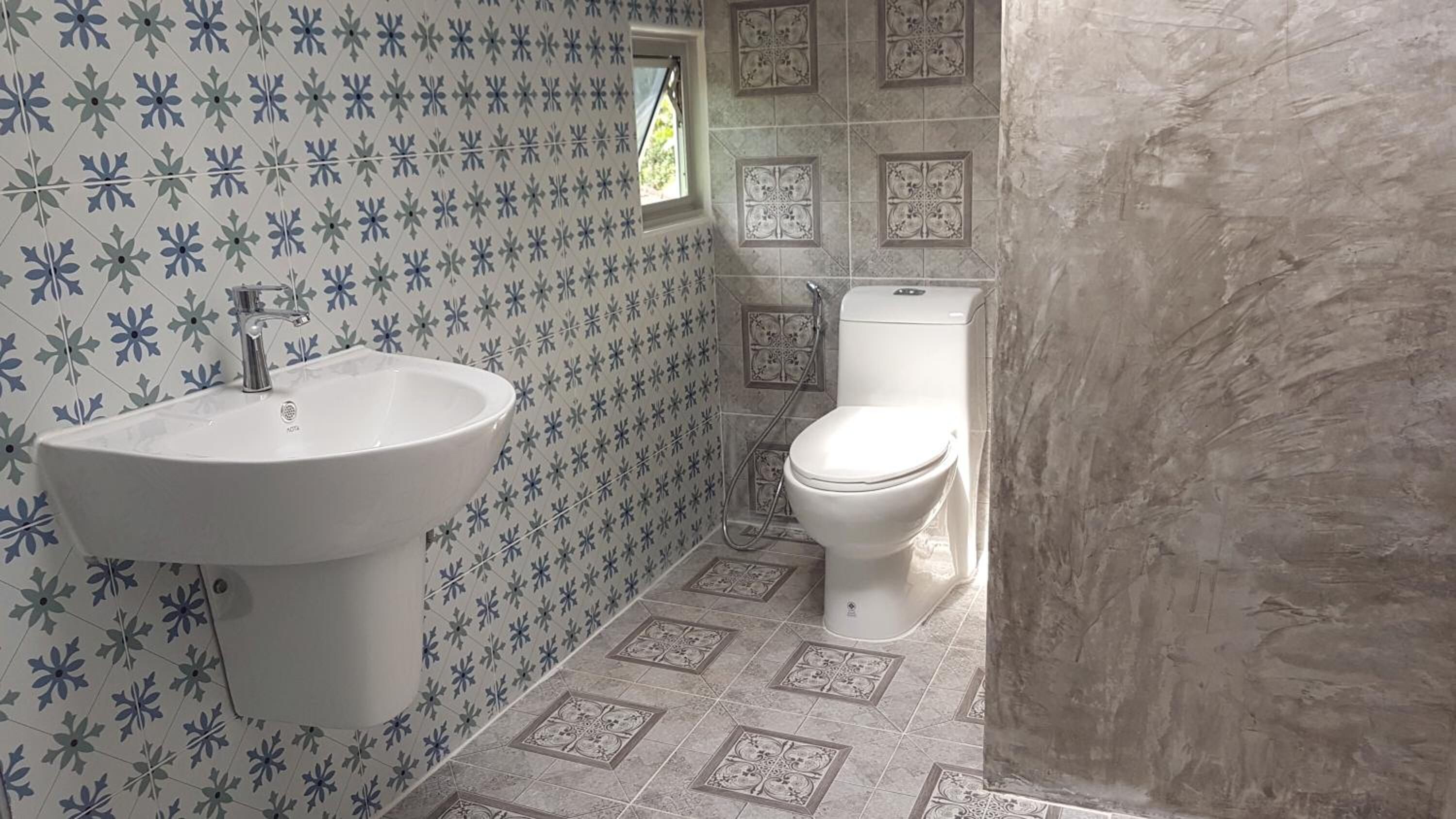 Casa de banho com lavatório, sanita e azulejos estampados.