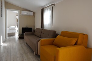 Sala de estar com sofá, poltrona, televisão e uma cama ao fundo.