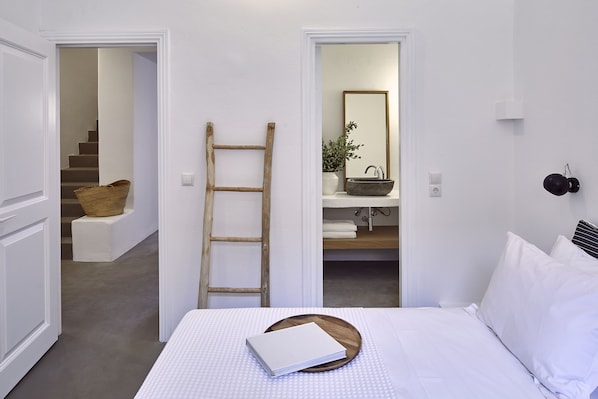 Quarto com cama, escada de madeira, cesta e banheiro visível por uma porta aberta.
