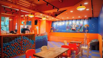 Um restaurante bem iluminado com decoração laranja e azul, com um balcão exibindo bolas azuis e laranjas, e um mural de um personagem de desenho animado.