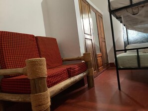 Um quarto com um banco de madeira, uma cama com mosquiteiro e uma porta de madeira.