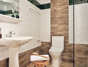 Um banheiro moderno com pia branca, vaso sanitário e um banquinho de madeira.