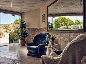 Um hall amplo com uma poltrona de couro, uma mesa redonda com uma xícara e uma grande janela com vista para áreas verdes e árvores.