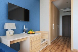 Quarto moderno com televisão de tela plana na parede, uma mesinha com abajur, uma cesta de frutas e uma garrafa de vinho.