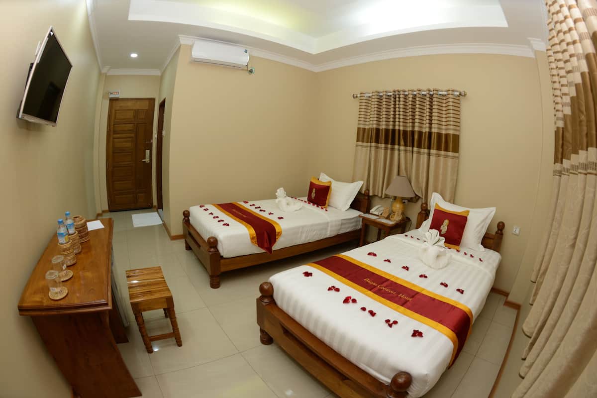 Quarto de hotel com duas camas, uma escrivaninha de madeira e uma televisão.