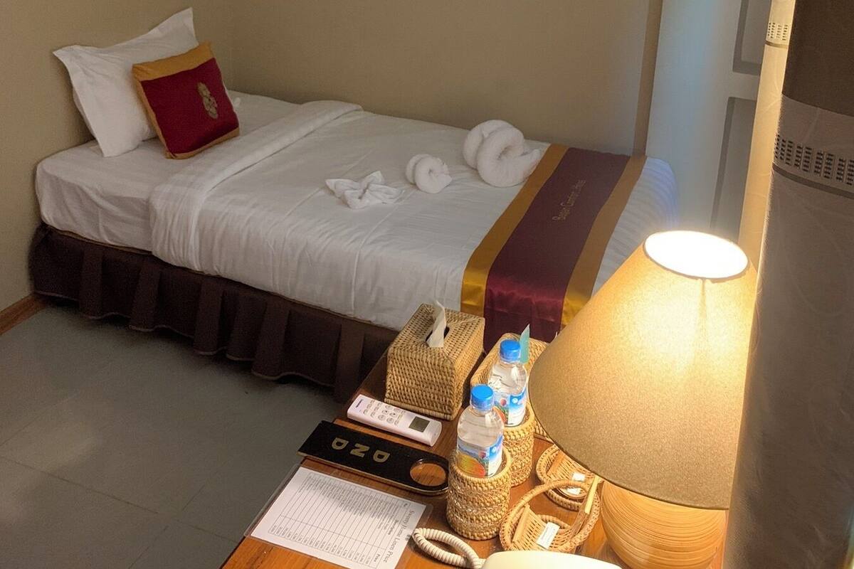 Quarto de hotel com cama bem arrumada, luminária, telefone, mesa pequena com caixa de lenços, garrafa de água e bloco de notas.