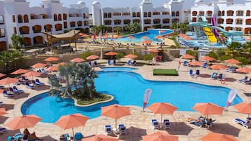 Uma área de piscina em resort com várias espreguiçadeiras e guarda-sóis, uma piscina central e um toboágua.