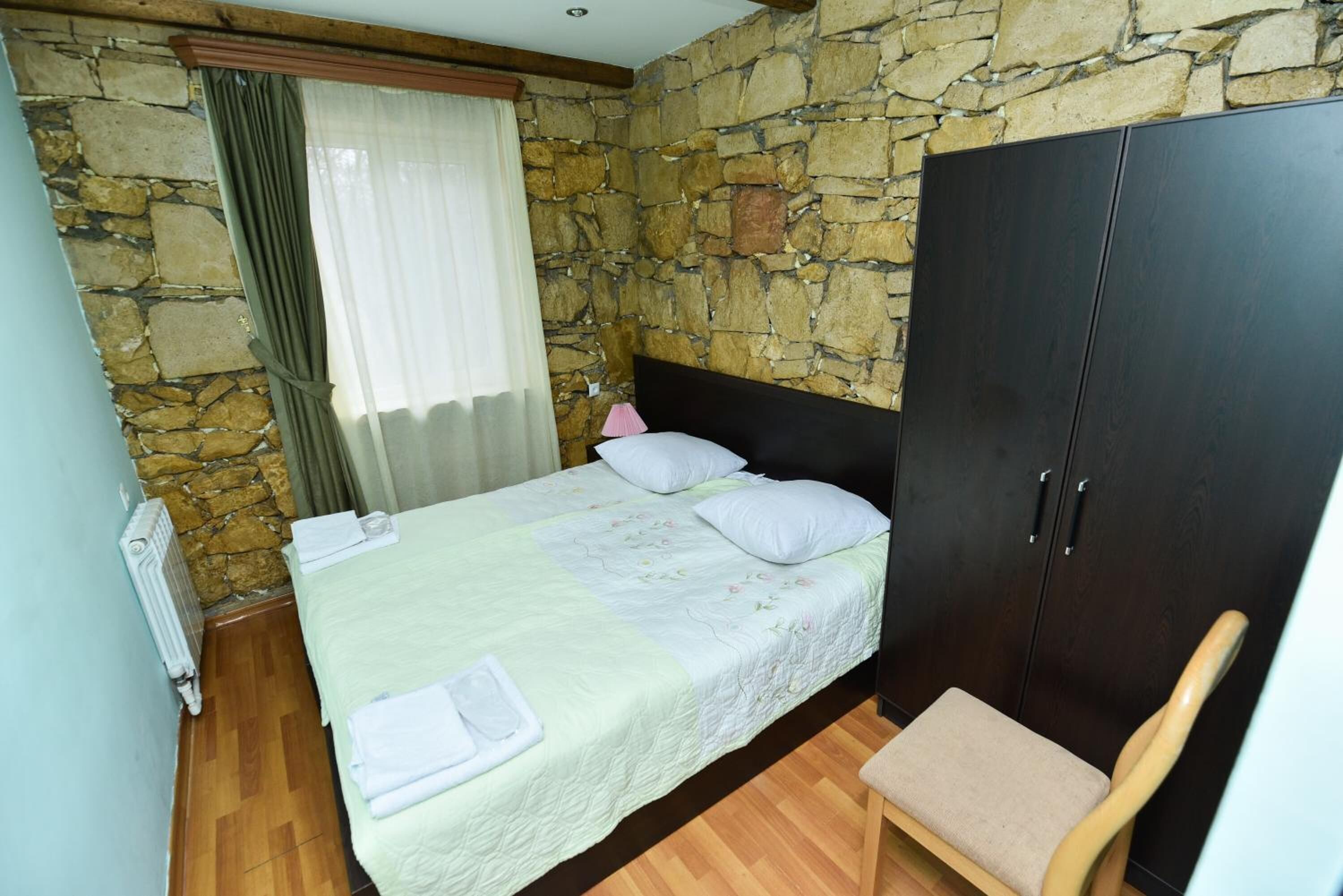 Quarto com cama, guarda-roupa, cadeira e janela com cortinas.