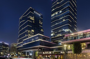 Um hotel moderno com uma placa grande Radisson Collection, janelas amplas e um restaurante visível chamado 'GUNAYDIN' no andar térreo.
