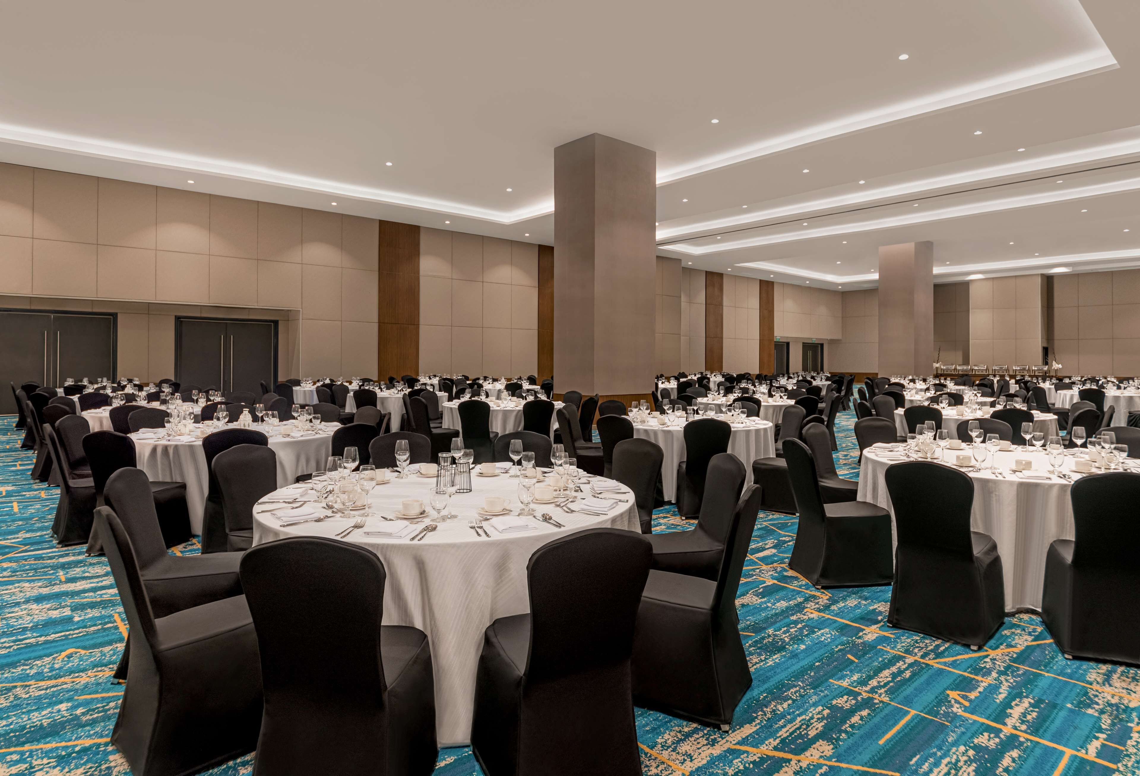 Amplo salão de banquetes com mesas redondas dispostas para refeições, equipado com cadeiras e louças.