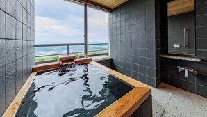 Casa de banho moderna com uma banheira grande, vista para o oceano e teto de madeira.