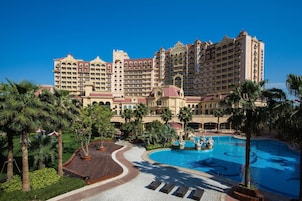 Um hotel grande com vários edifícios, piscina central e palmeiras.