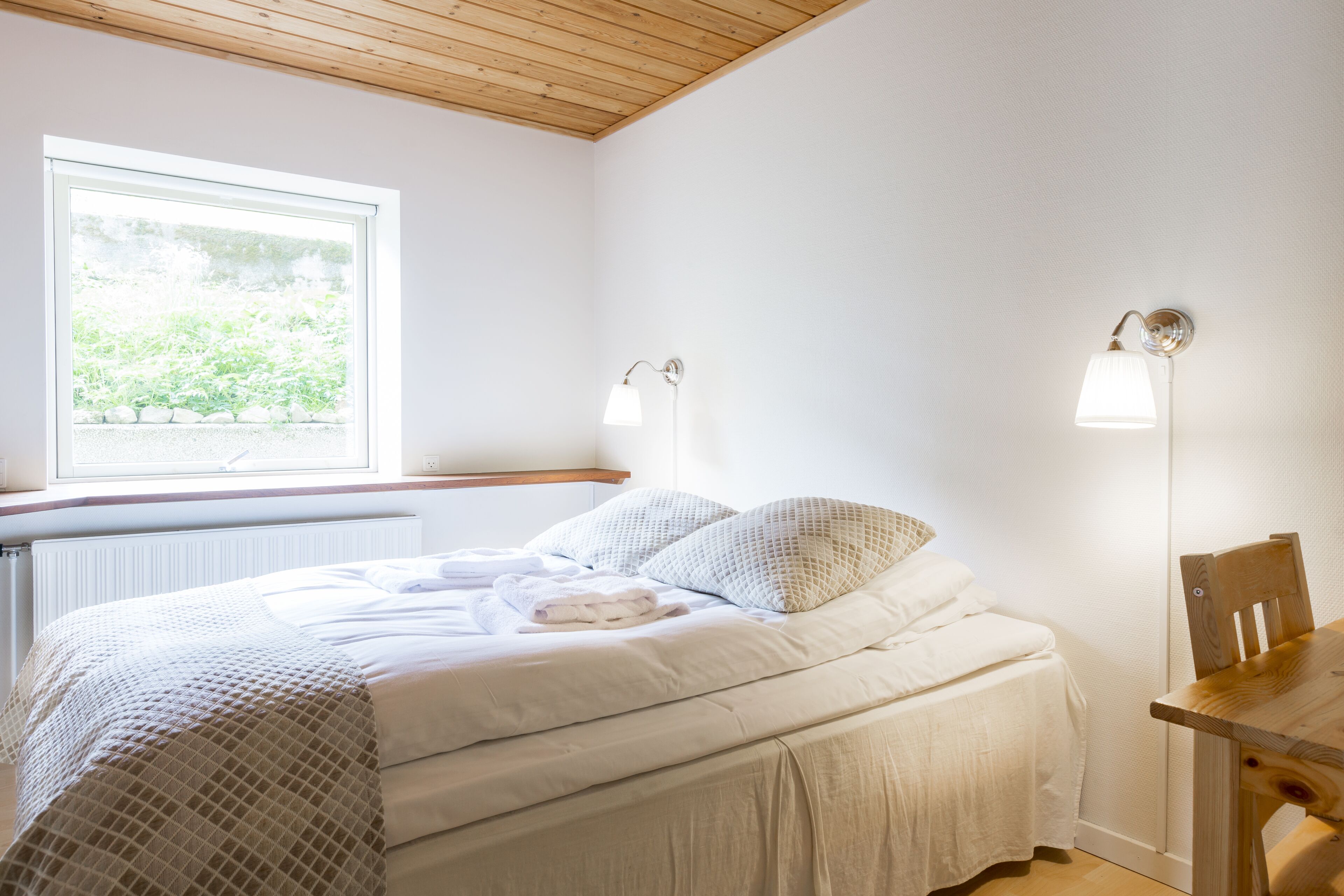 Quarto com cama, mesa de cabeceira, abajur e janela.
