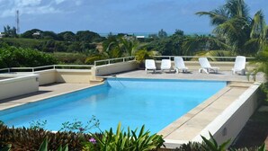 Piscina com cadeiras de sol brancas e vista para o oceano.